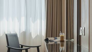 Quarto de hotel moderno com uma secretária preta, uma cadeira, uma lâmpada e uma janela com cortinas.