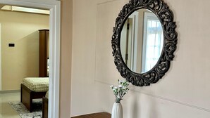 Um corredor com um banco de madeira, um vaso branco com flores e um espelho ornamentado na parede.