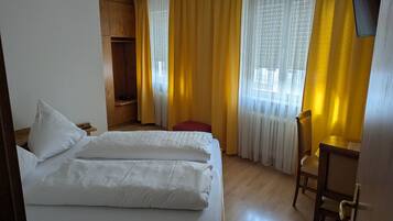 Um quarto com uma cama, um guarda-roupa de madeira, um banquinho vermelho e uma cadeira.