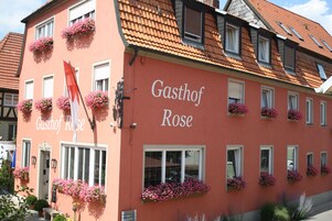 Um edifício com a fachada identificada como "Gasthof Rose", com várias janelas adornadas com caixas de flores e um telhado de telhas tradicionais.