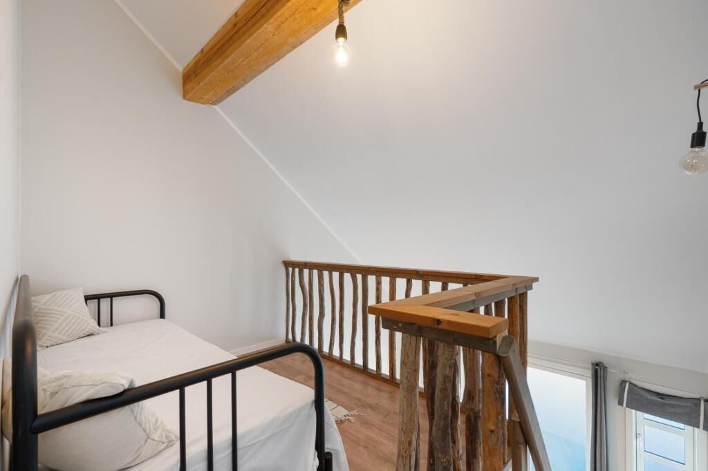 Quarto com cama, cabeceira de madeira e corrimão de escada de madeira.