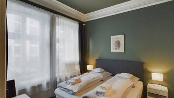 Quarto de hotel com uma cama, duas mesas de cabeceira, uma janela com cortinas translúcidas e um quadro na parede.