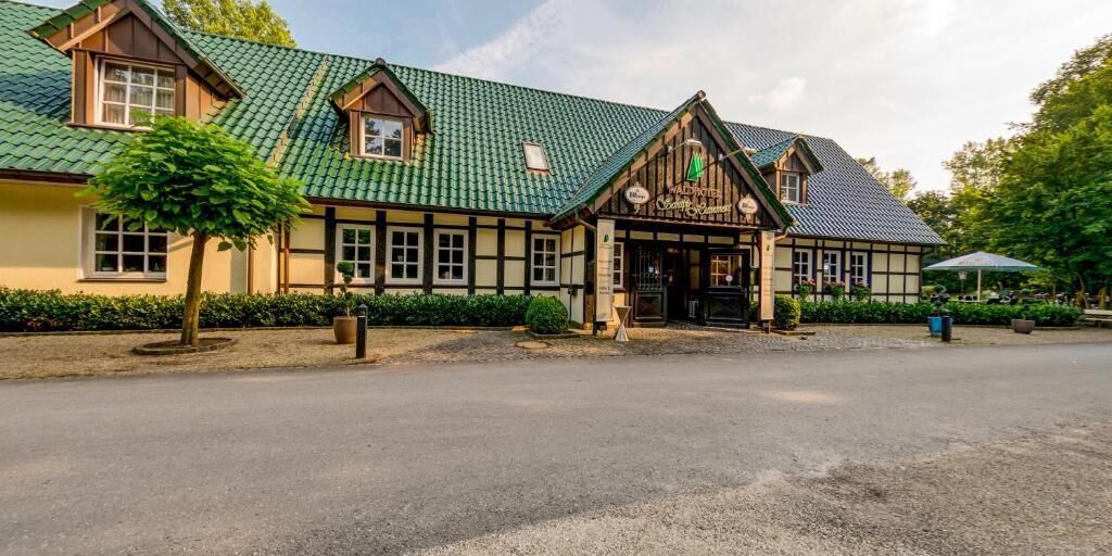 Um edifício tradicional com telhado verde, entrada central e uma pequena árvore em frente.