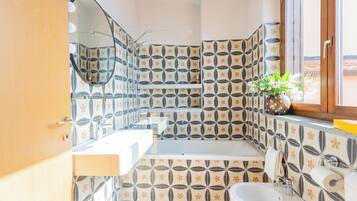 Um banheiro com azulejos estampados, um espelho, uma pia, um bidê e uma janela com vista.