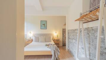 Quarto com cama, mesas de cabeceira, luminária na parede, cabideiro de madeira e quadro na parede.