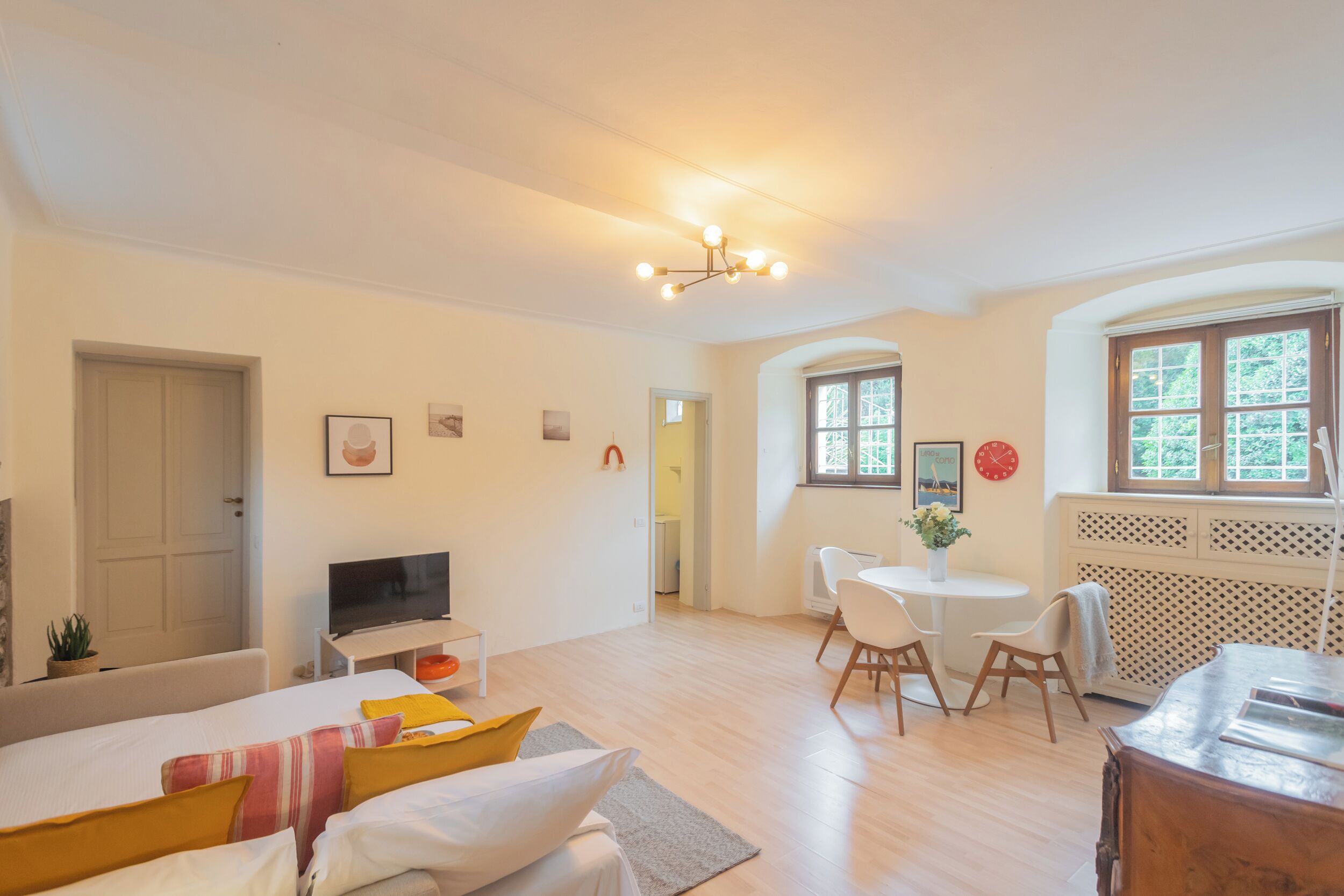 Uma sala de estar moderna com sofá, televisão, mesa de jantar e cadeiras. Há uma porta, janelas e um radiador.