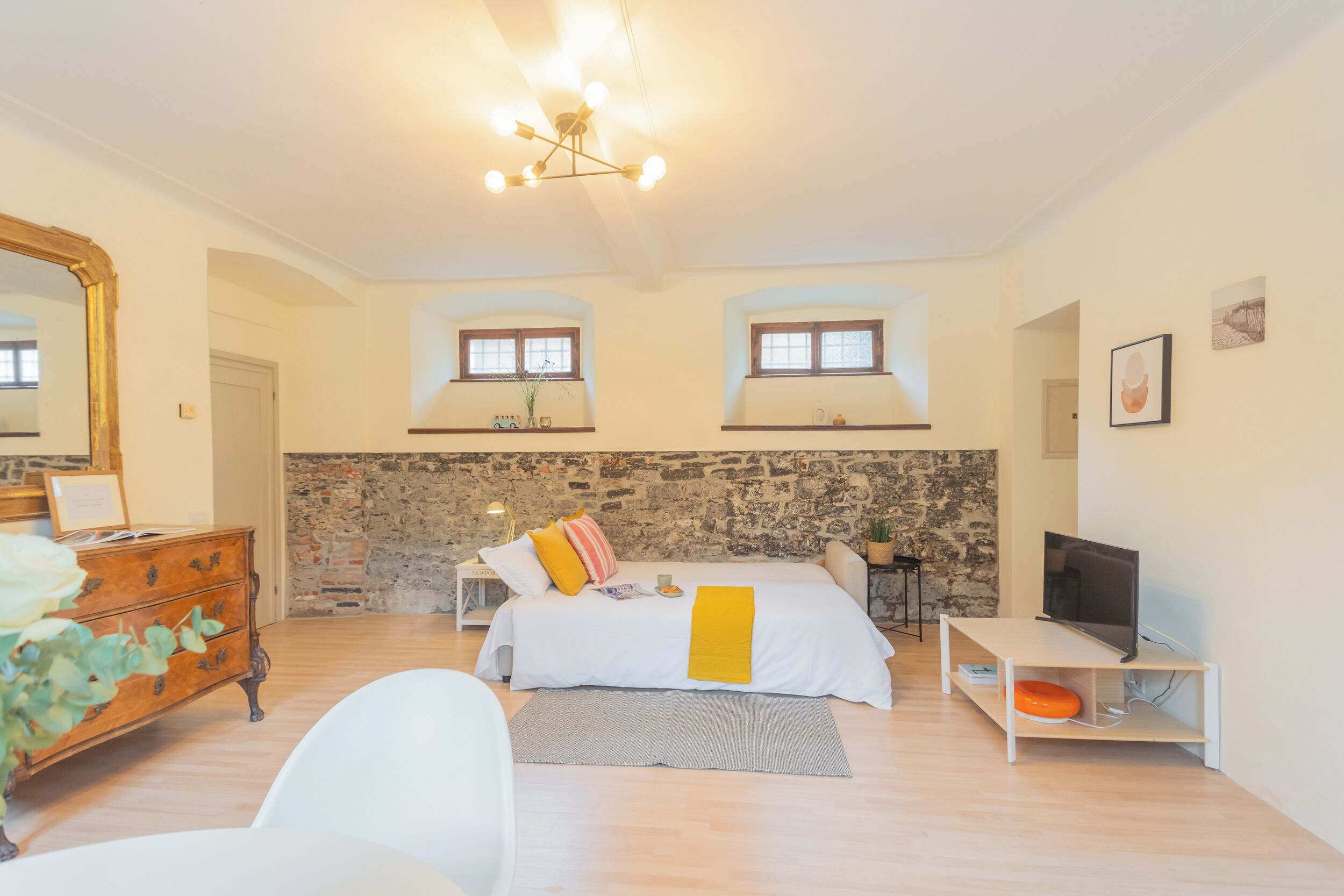 Quarto com cama, cómoda, televisão e parede de pedra.