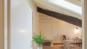 Quarto com sofá branco, uma mesinha com abajur, tapete branco e planta em pote de vidro.