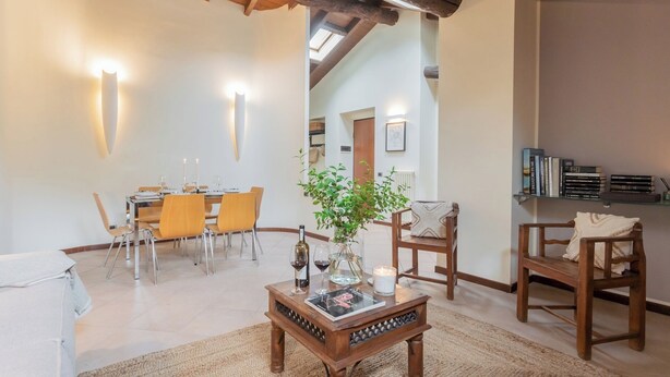 Uma sala de estar aconchegante com área de jantar, vigas de madeira, lareira e estante de livros.