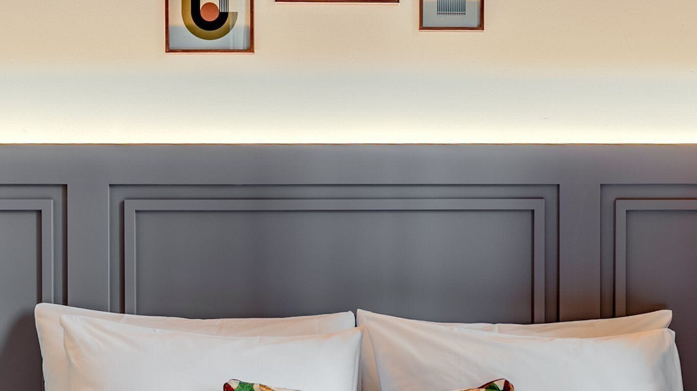 Quarto de hotel com cabeceira cinzenta, duas almofadas brancas e uma obra de arte emoldurada sobre a cama.
