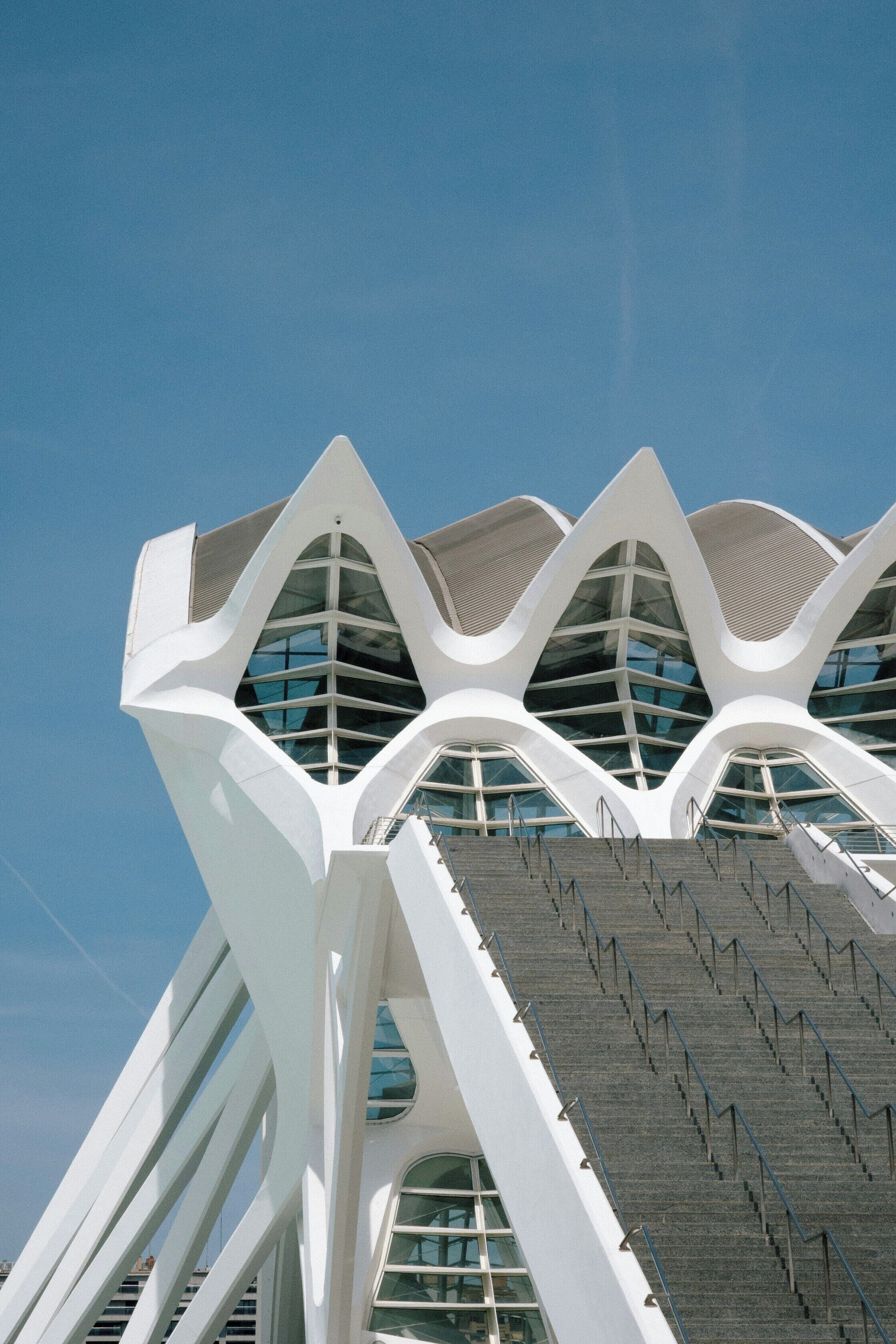 Um edifício de arquitetura moderna com design geométrico único, apresentando uma série de estruturas angulares e sobrepostas e uma escadaria imponente que leva a um nível superior.