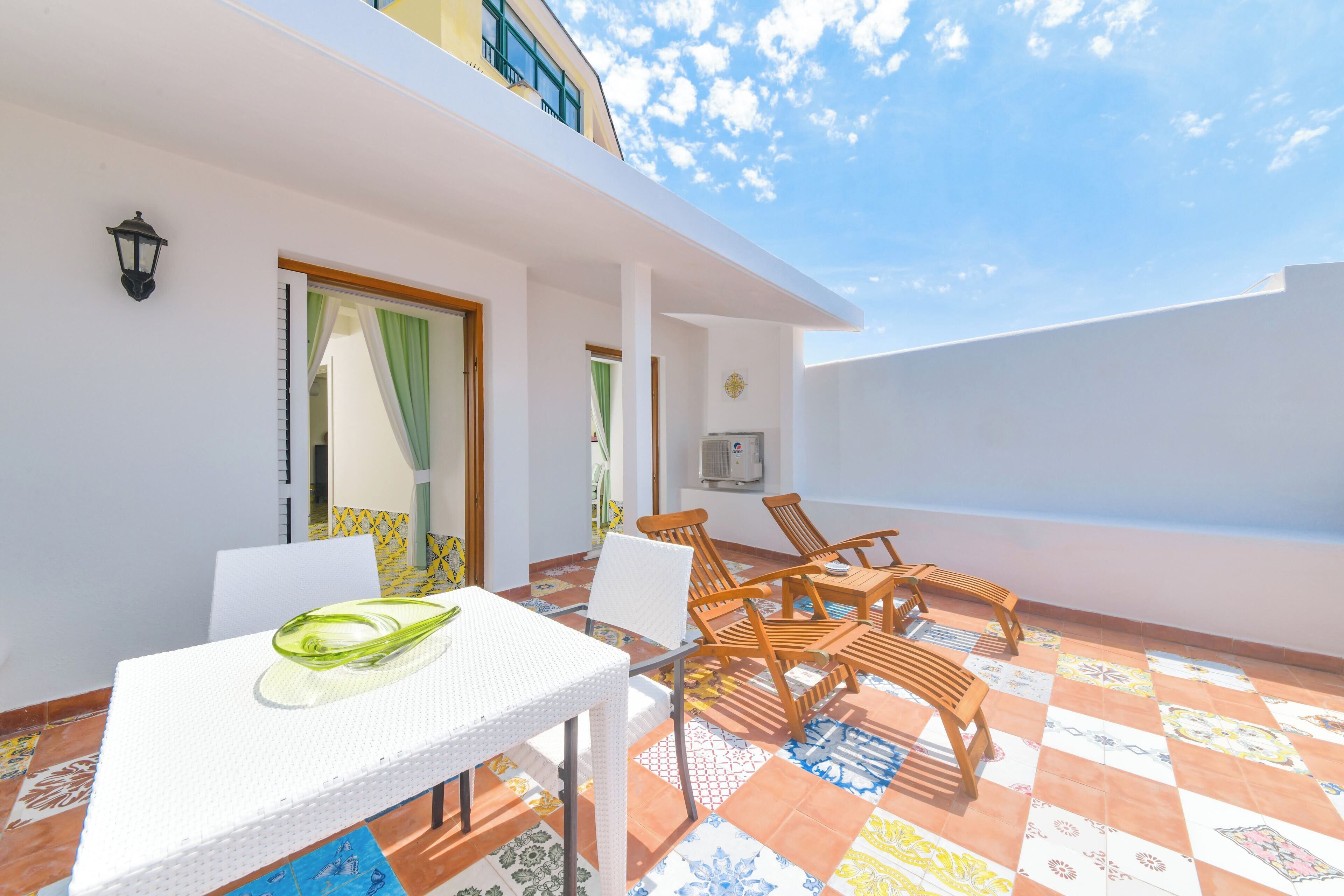 Terraço com mesa e cadeiras brancas, piso estampado e vista do céu.