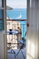 Vista de um veleiro no mar, partindo de uma varanda com arquitetura de pedra e guarda-corpo de metal.