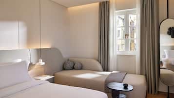 Quarto de hotel moderno com cama, sofá, uma mesinha e janela com cortinas.