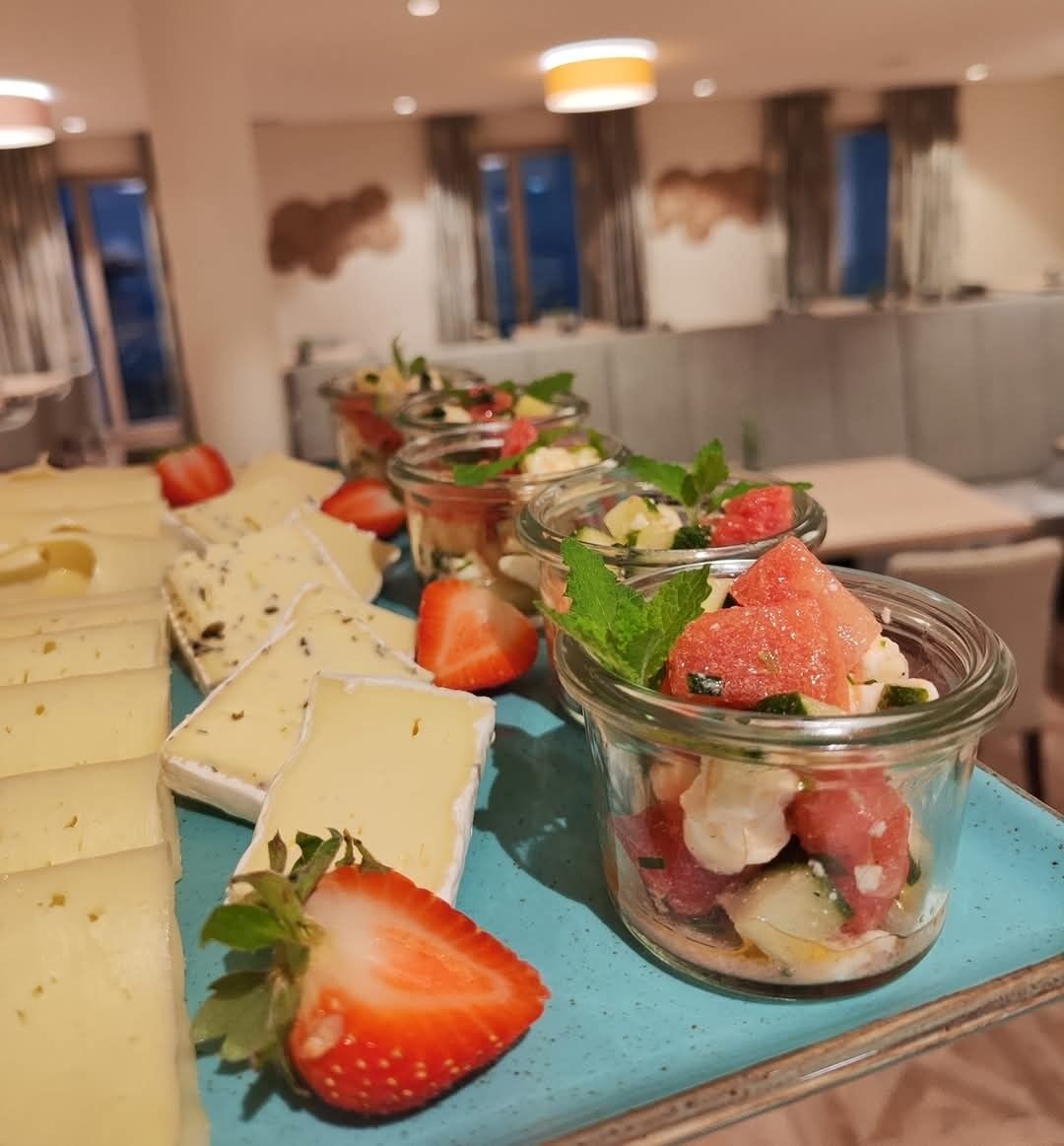 Mesa de buffet com diversos queijos e sobremesas com frutas em potes de vidro.