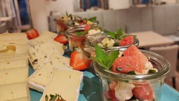 Mesa de buffet com diversos queijos e sobremesas com frutas em potes de vidro.