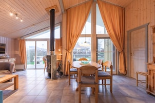 Interior de madeira com uma mesa de jantar, cadeiras, lareira e janelas amplas.