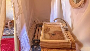 Um quarto com tenda, pia de madeira, cortinas brancas e um espelho pendurado.
