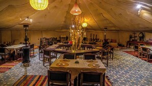 Uma área de refeições estilo tenda, com mesas redondas, cadeiras e luminárias pendentes.