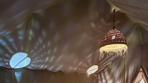 Um quarto aconchegante e bem iluminado, com uma cama grande, luminária pendente e vista para o exterior através de uma janela.