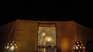 Uma tenda com a porta aberta, mostrando um espaço com mesas e cadeiras, e um lustre pendurado.