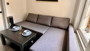 Um espaço de estar moderno e compacto, com um sofá modular, uma mesinha com pratos e copos, e um espelho na parede.