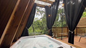 Uma banheira de hidromassagem numa varanda de madeira com vista para árvores.