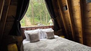 Quarto com cama, cortinas, piso xadrez e vista para árvores e um carro na rua.