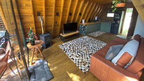 Uma sala de estar acolhedora no sótão, com vigas de madeira, lareira, televisão, sofá e um espaço de cozinha.