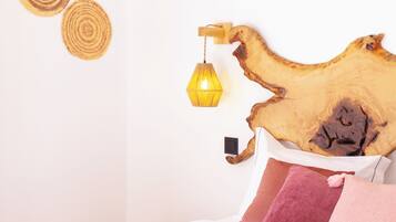 Uma cama com cabeceira de madeira, duas decorações de parede feitas de fibras naturais e um abajur amarelo fixado na parede.