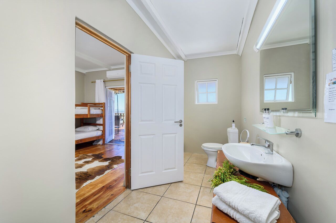 Uma casa de banho com soalho de madeira, uma sanita branca, uma loiça e uma porta que dá para um quarto com uma cama dupla.