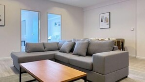 Uma sala de estar moderna com um sofá modular cinza, uma mesa de centro de madeira e uma pequena mesa lateral de madeira.