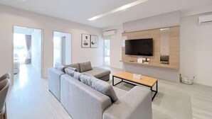 Uma sala de estar moderna com um sofá seccional cinza, uma mesa de centro e uma TV de tela plana fixada na parede.