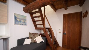 Uma sala de estar acolhedora com um sofá cinza escuro, almofadas estampadas, uma escada de madeira e uma porta de madeira.