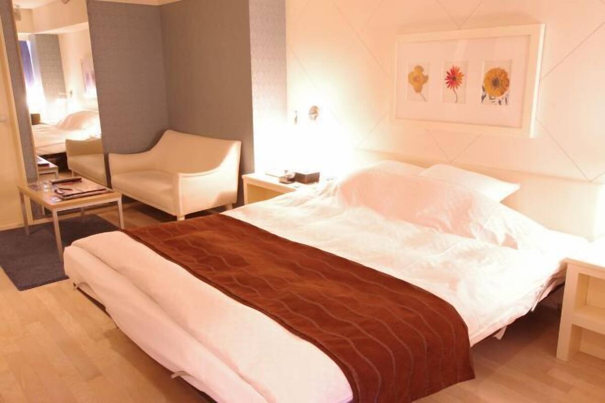 Quarto de hotel com cama, cadeira, mesa de cabeceira e uma obra de arte na parede.
