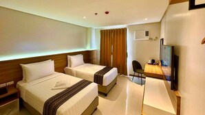 Quarto de hotel com duas camas, uma escrivaninha, uma cadeira, uma televisão e um aparelho de ar condicionado.