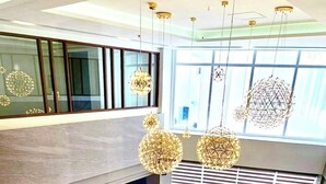 Um saguão de hotel com balcão de recepção, área de estar e um amplo espaço aberto com teto alto e luminárias esféricas penduradas.
