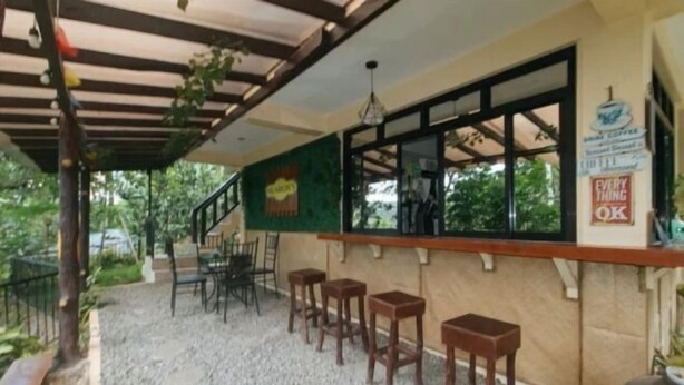 Uma área de estar externa com bancos e mesas de madeira, um alpendre coberto e vista para o verde.