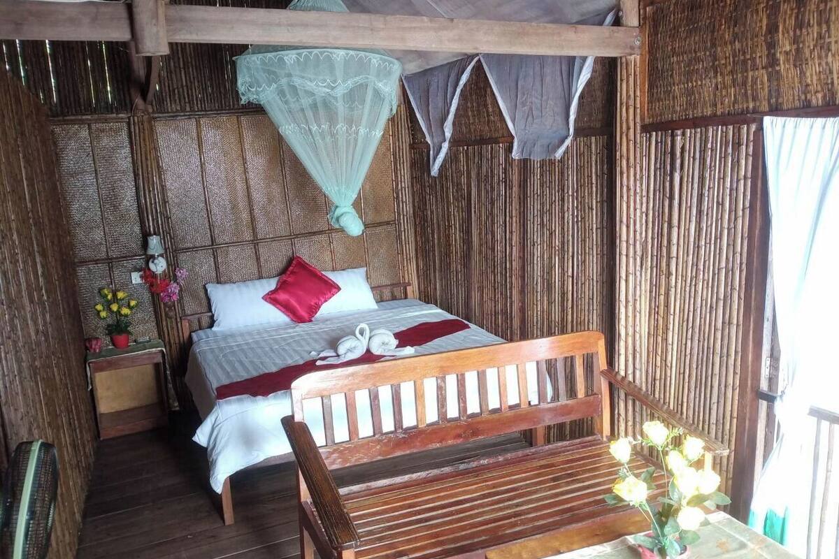 Um quarto de madeira com uma cama, um banco e uma pequena mesa com flores.