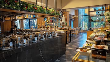 Espaço de buffet com diversas estações de comida, variedade de pratos e vista para o exterior através de amplas janelas.
