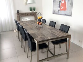 Uma mesa de jantar com seis cadeiras, uma cesta de frutas, um abajur e um quadro na parede.