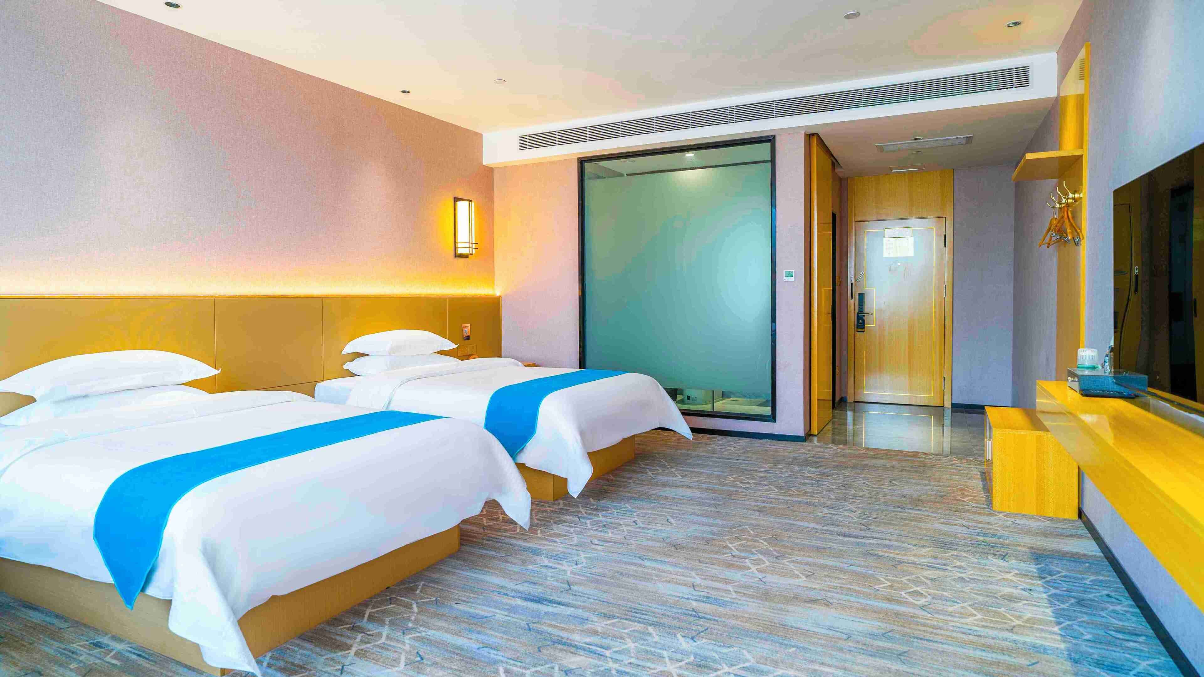 Quarto de hotel com duas camas, uma televisão grande e uma porta de correr de vidro que dá para um banheiro.