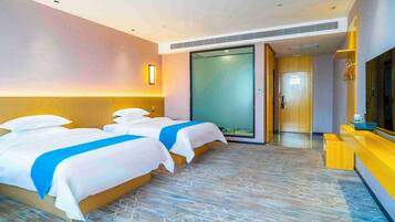 Quarto de hotel com duas camas, uma televisão grande e uma porta de correr de vidro que dá para um banheiro.