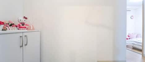 Quarto com guarda-roupa branco, uma mesa pequena e cama com roupa de cama rosa.
