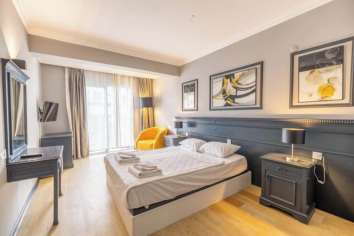 Quarto de hotel com uma cama grande, uma escrivaninha, uma cadeira e obras de arte nas paredes.