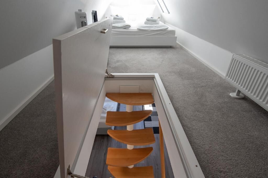 Quarto de hotel moderno com porta deslizante integrada que dá para uma cama, um radiador e uma janela pequena.