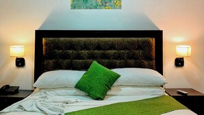 Quarto de hotel com uma cama grande, almofadas de lançamento verdes, um cobertor verde e uma obra de arte floral sobre a cama.