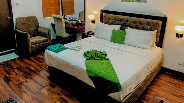 Quarto de hotel com cama, cadeira, escrivaninha, espelho e uma obra de arte na parede.