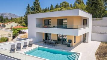 Uma casa moderna de dois andares com piscina, área de estar externa e montanhas ao fundo.