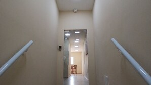 Um corredor estreito e bem iluminado, com piso de madeira e paredes brancas, que leva a um quarto com uma mesa pequena e cadeiras.